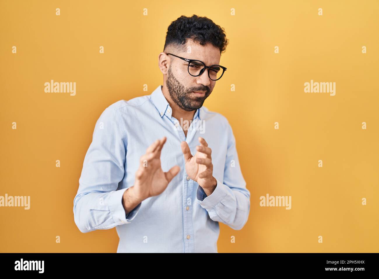 Hispanic man with beard standing over yellow background disgusted ...