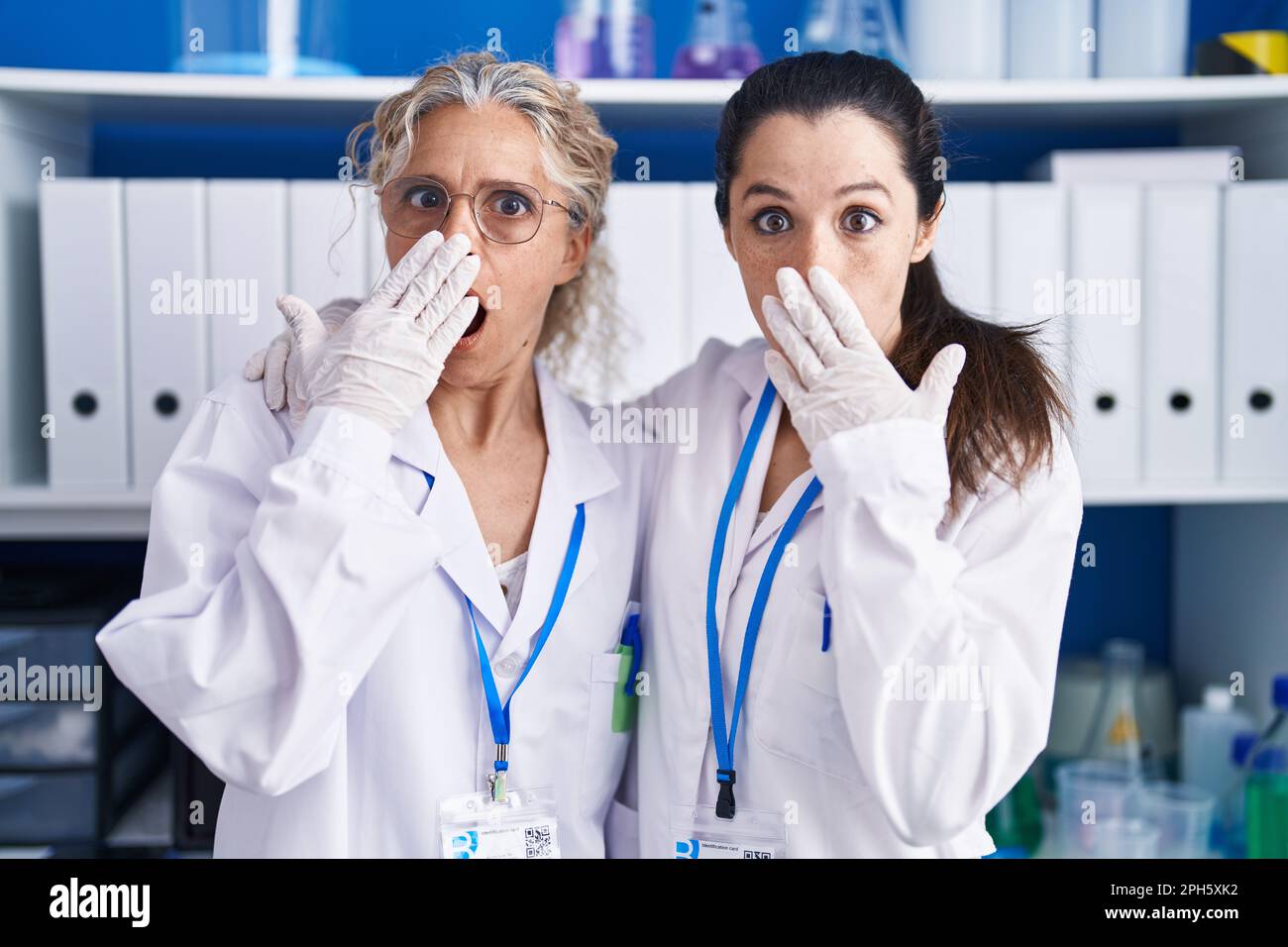 Mother and daughter working at scientist laboratory covering mouth with ...