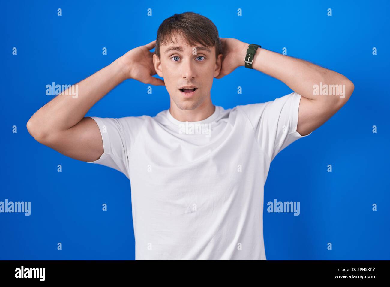 Caucasian blond man standing over blue background crazy and scared with ...