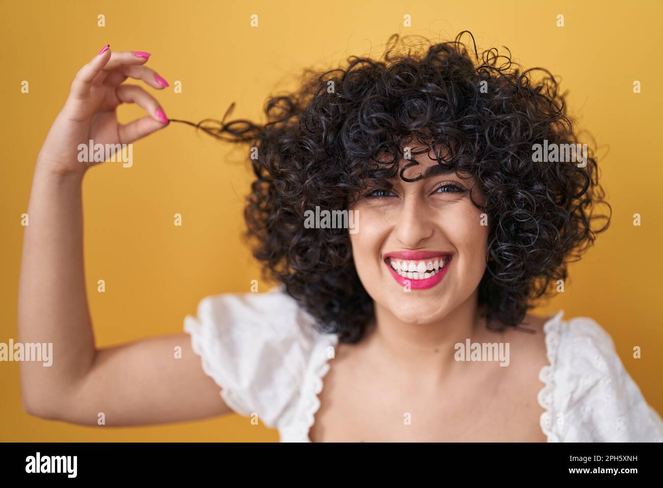 Young brunette woman with curly hair holding curl smiling and laughing hard out loud because ...