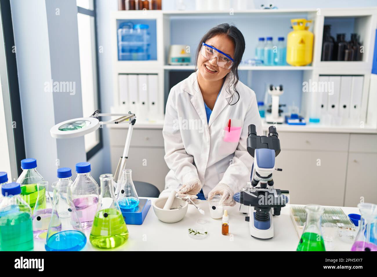 Young chinese woman wearing scientist uniform working at laboratory ...