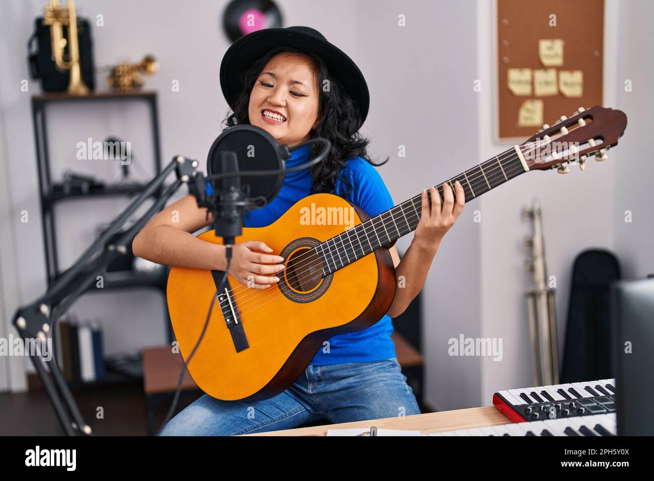 Young chinese woman artist singing song playing guitar at music studio ...