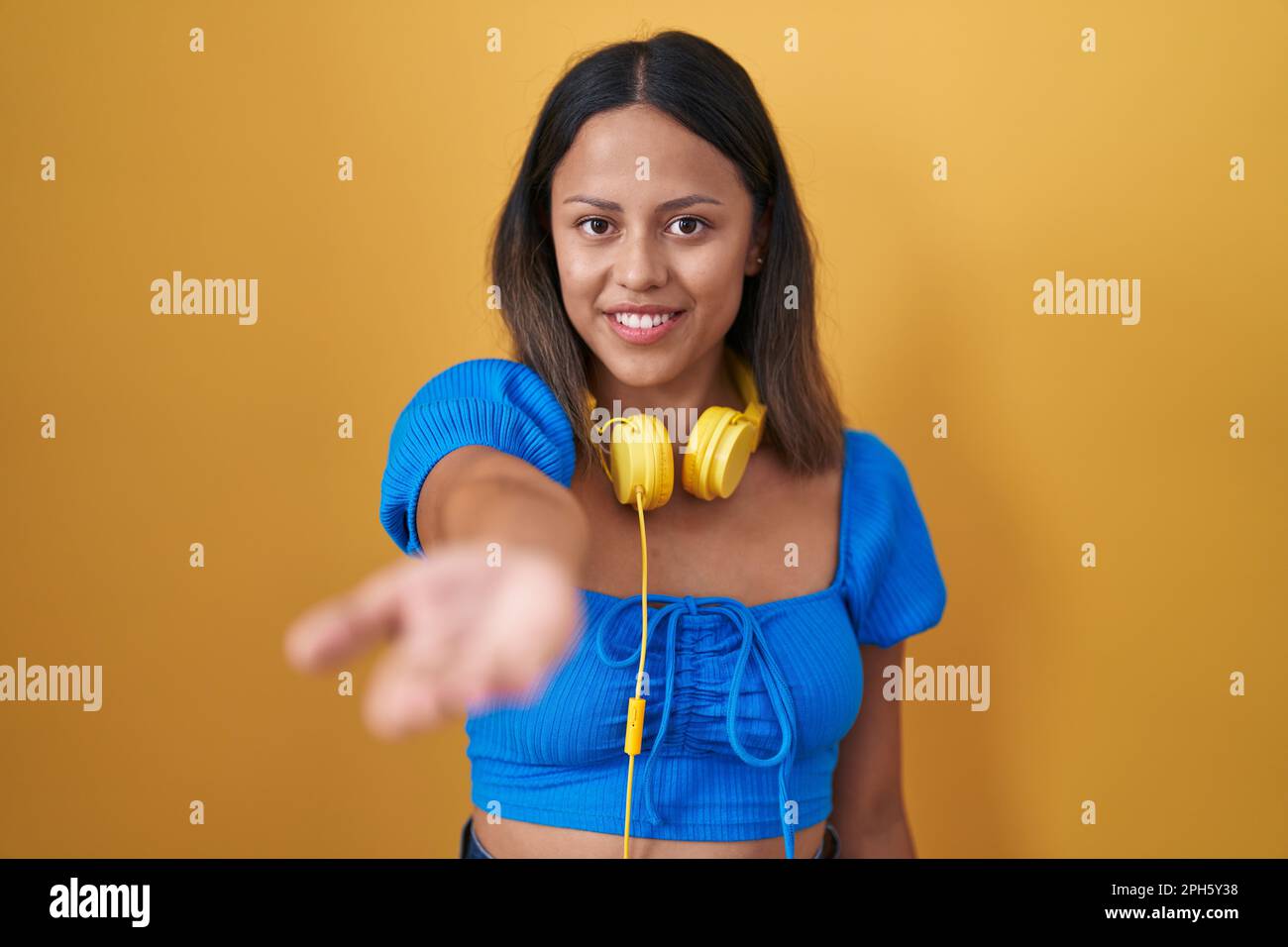 Hispanic young woman standing over yellow background smiling cheerful ...