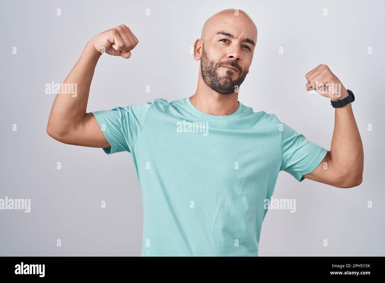 Middle age bald man standing over white background showing arms muscles ...