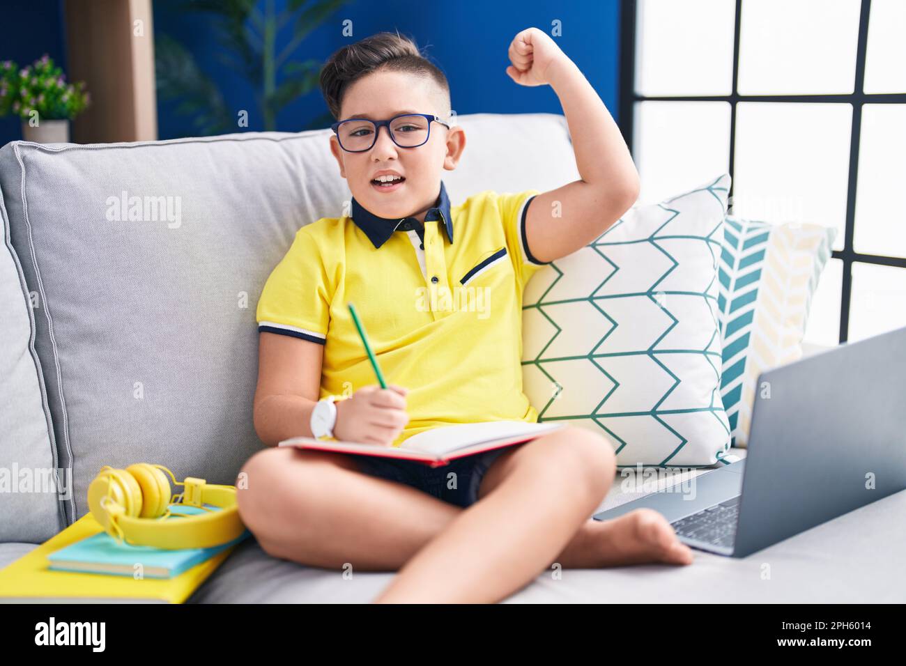 Young hispanic kid doing homework sitting on the sofa angry and mad ...