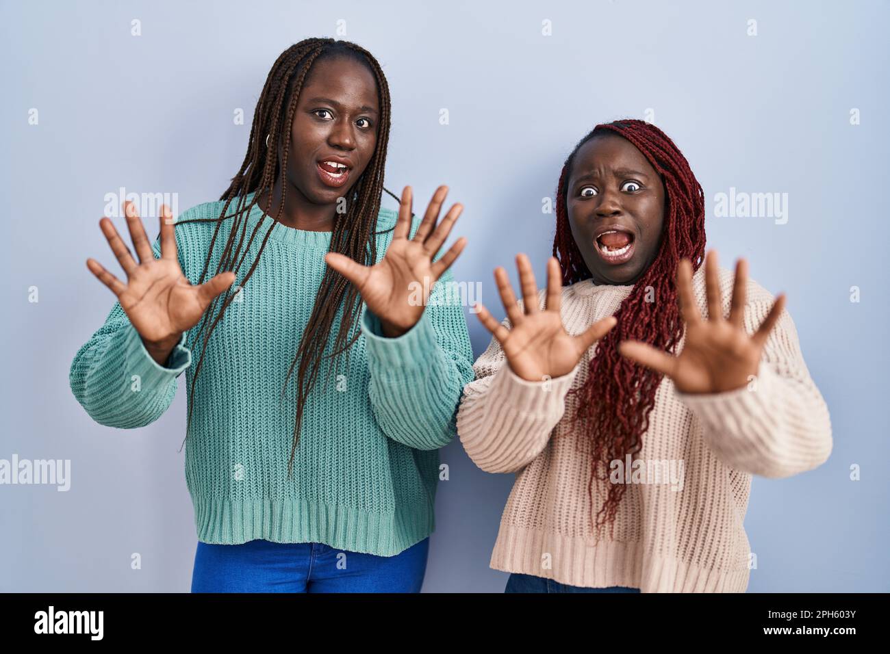 Two african woman standing over blue background afraid and terrified ...