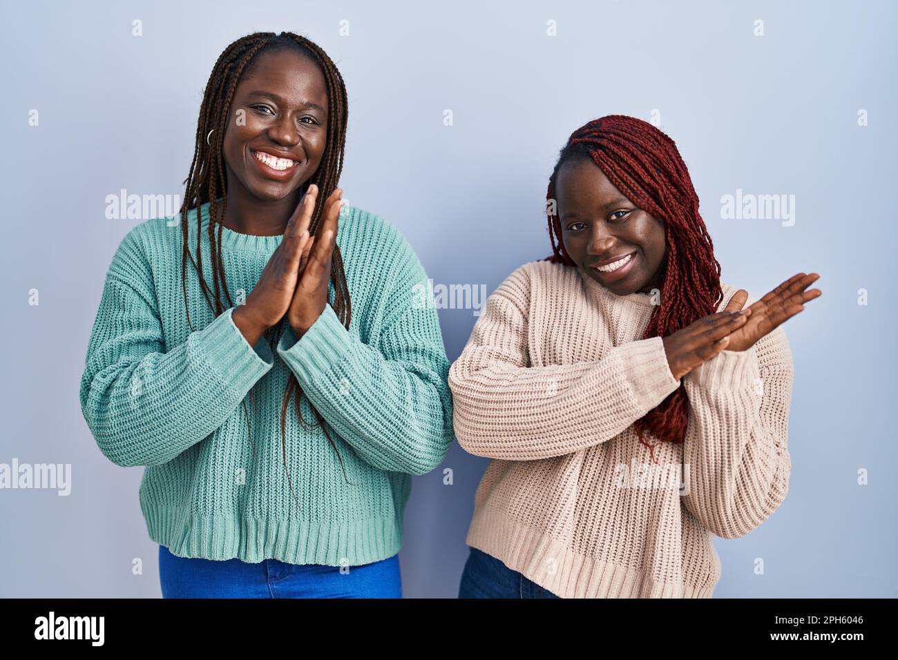 Two african woman standing over blue background clapping and applauding ...