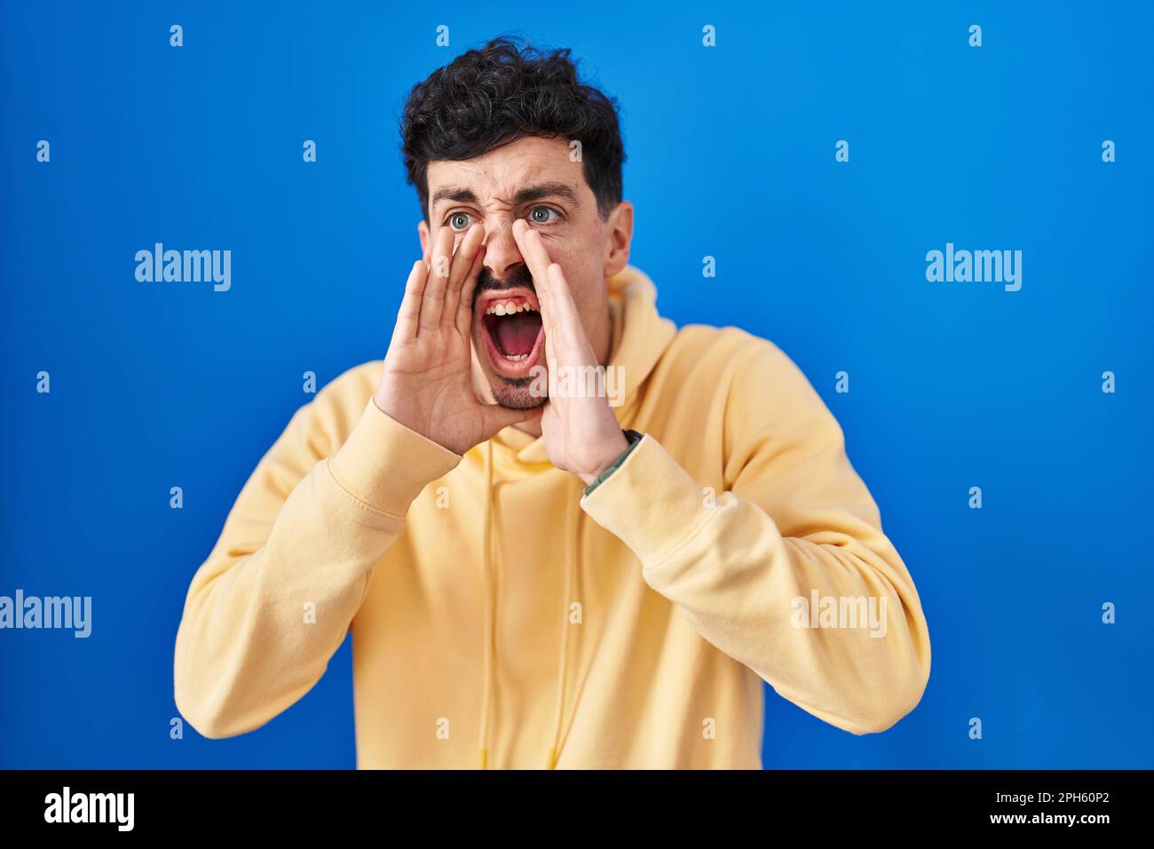 Hispanic man standing over blue background shouting angry out loud with ...