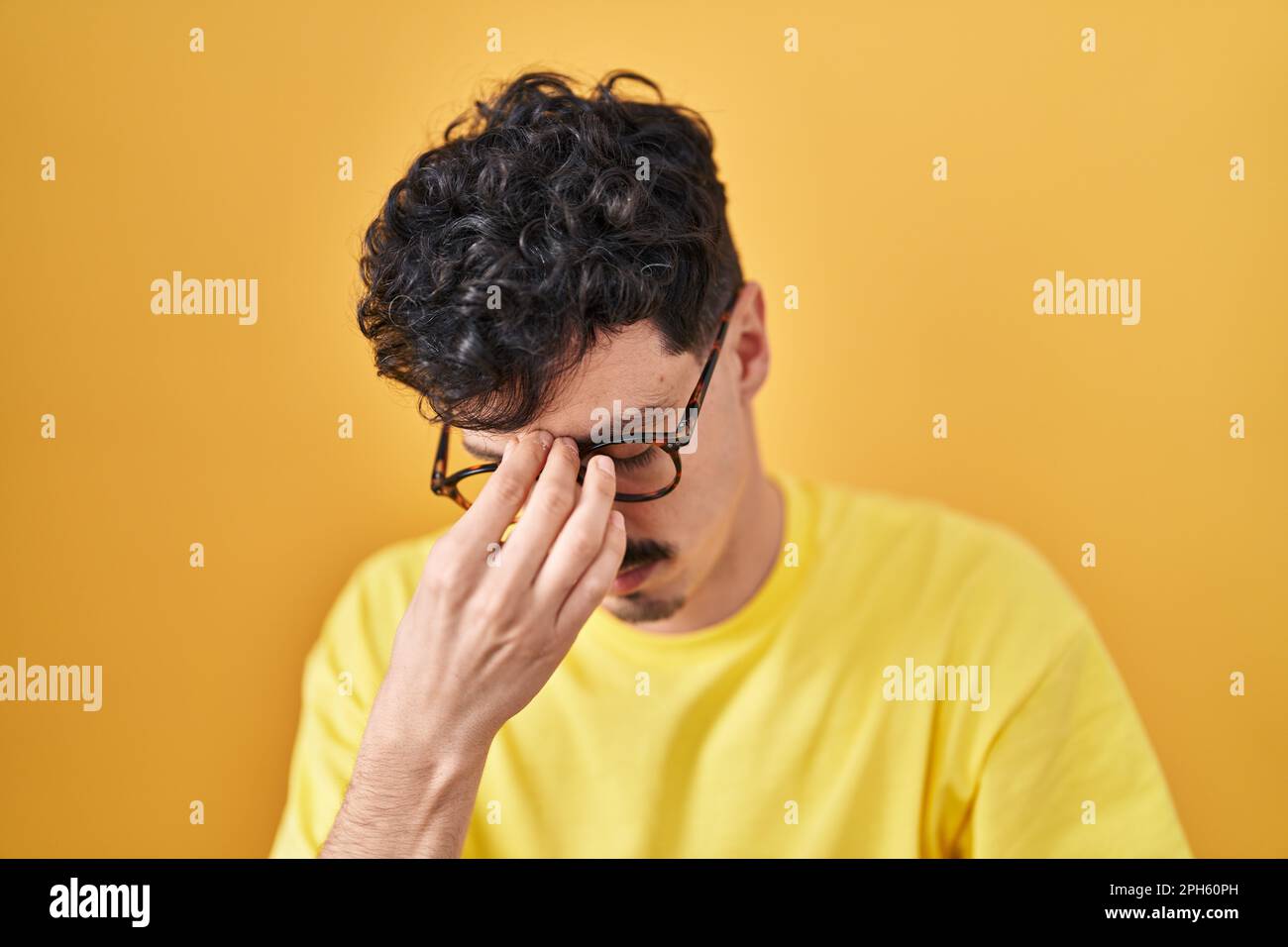 Hispanic man wearing glasses standing over yellow background tired ...
