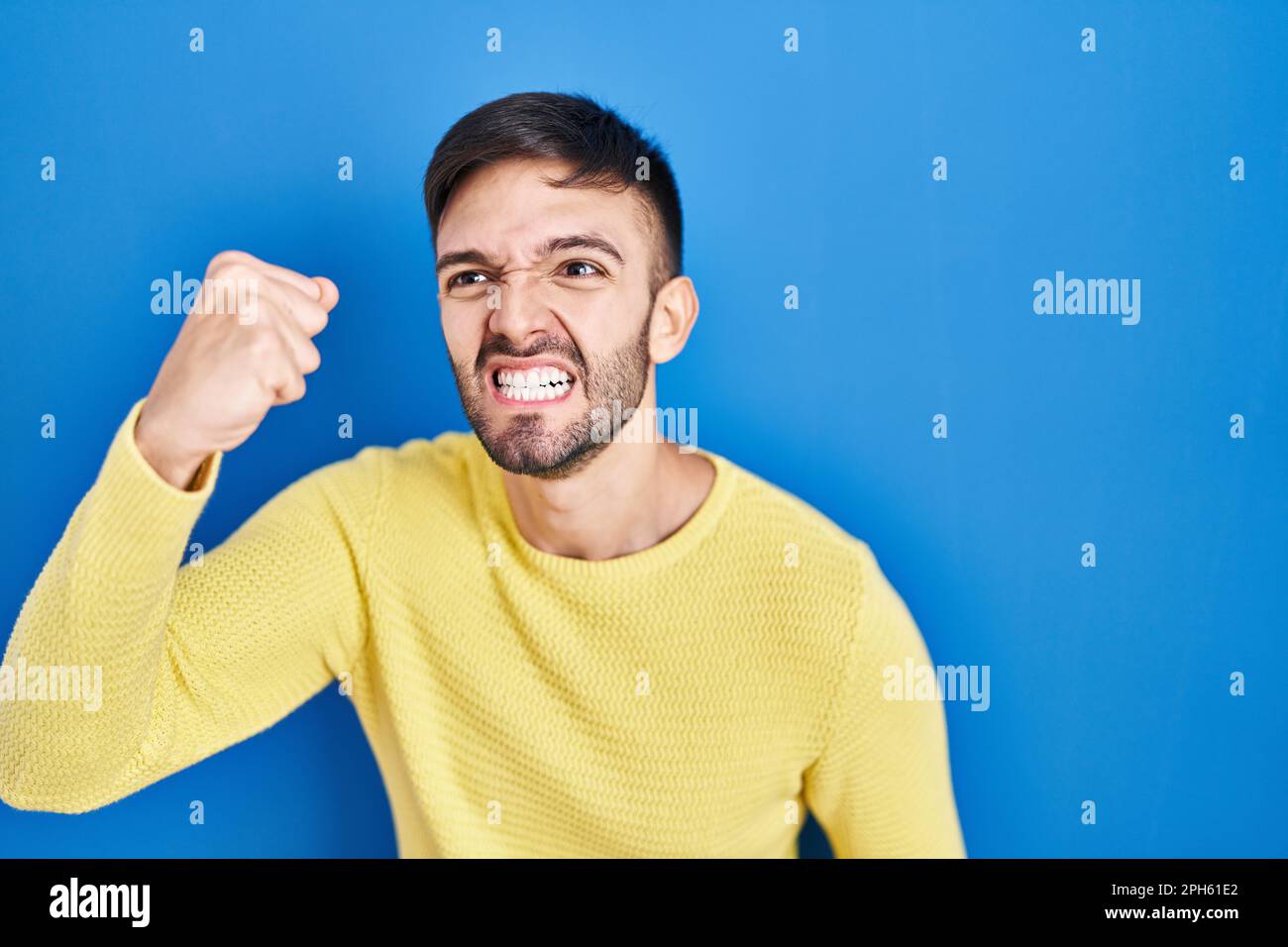 Hispanic man standing over blue background angry and mad raising fist ...