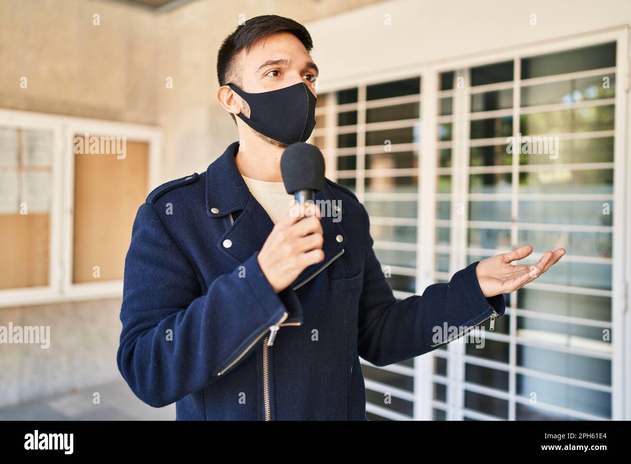 Young hispanic man reporter wearing medical mask working using microphone at street Stock Photo ...