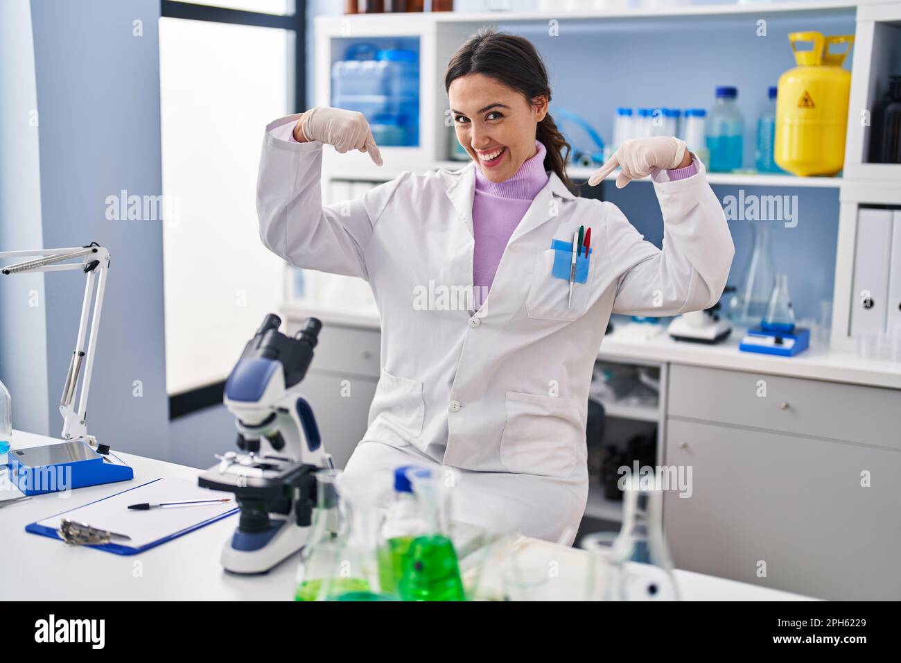 Young brunette woman working at scientist laboratory looking confident with smile on face ...
