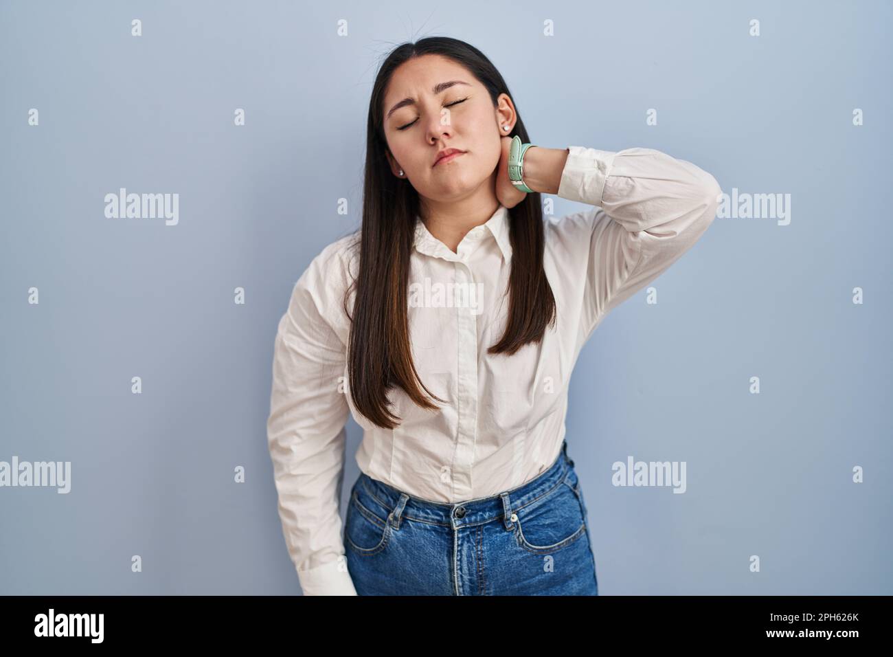 Young latin woman standing over blue background suffering of neck ache ...