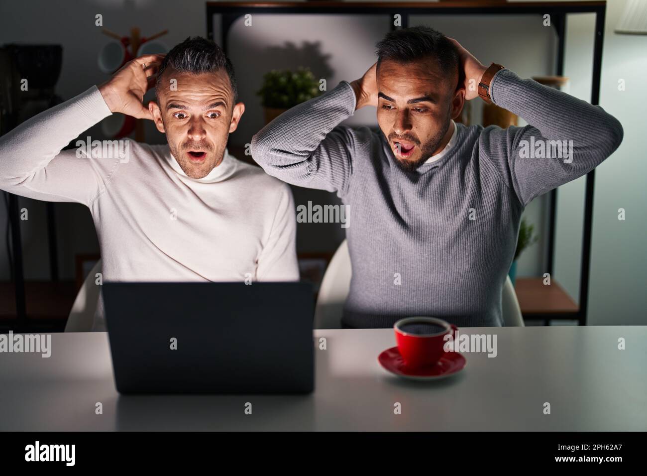 Homosexual couple using computer laptop crazy and scared with hands on ...
