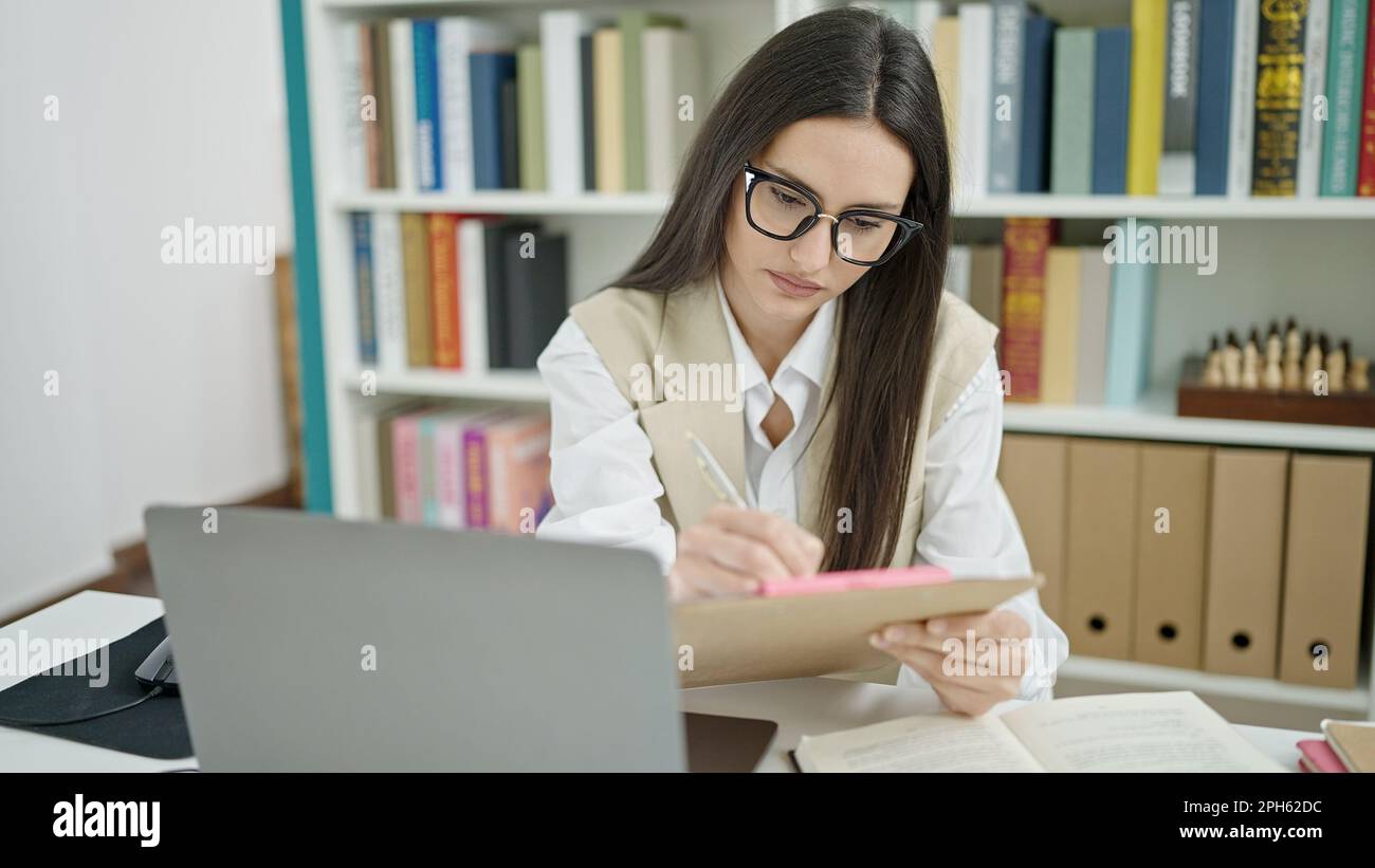 Young beautiful hispanic woman student stressed writing on document at ...