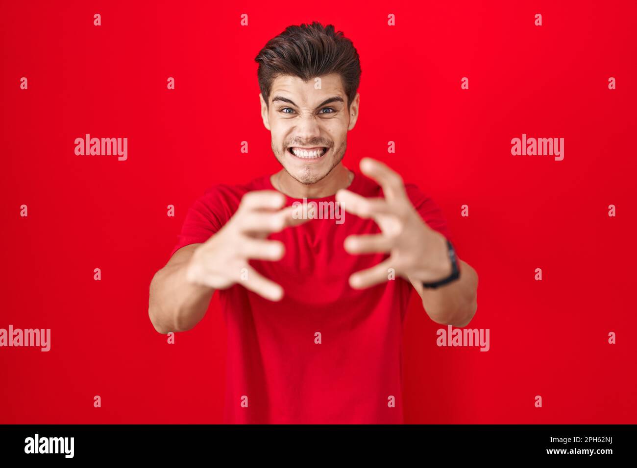 Young hispanic man standing over red background shouting frustrated ...