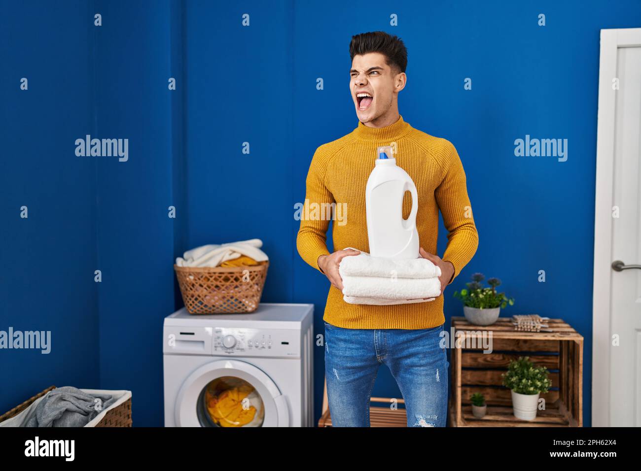 Young hispanic man holding clean towels angry and mad screaming ...