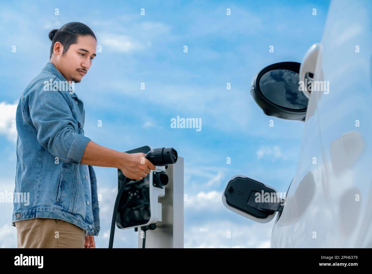 Progressive man with electric vehicle and cloudscape background. EV car ...