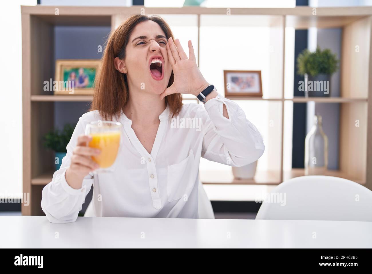 Brunette woman drinking glass of orange juice shouting and screaming ...