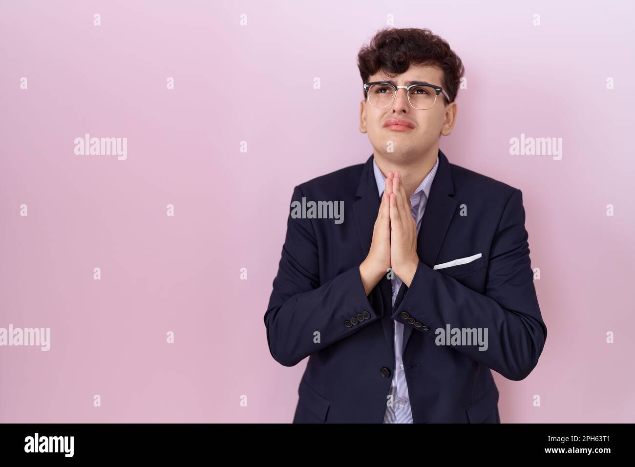 Young non binary man with beard wearing suit and tie begging and ...