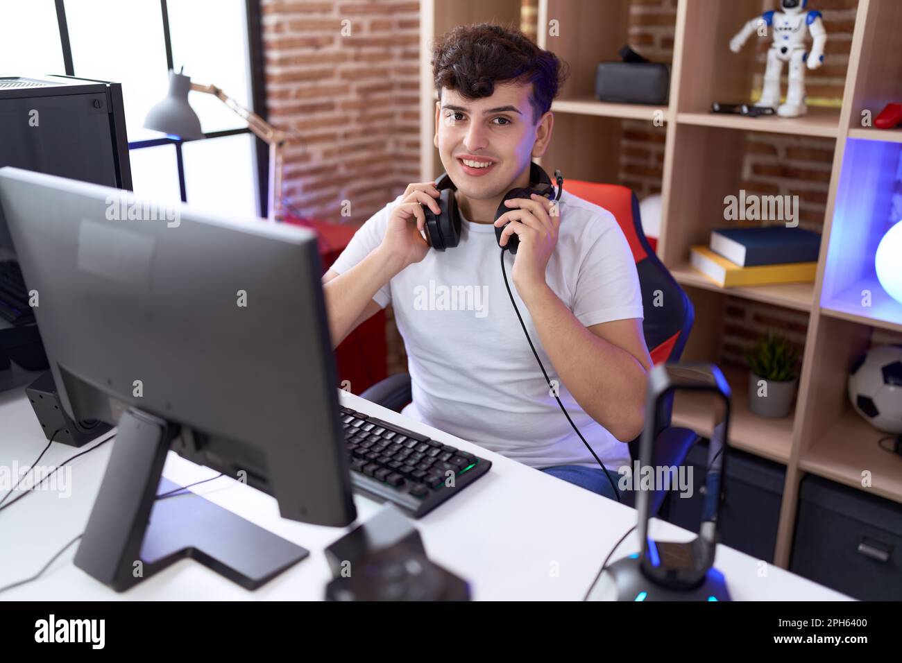 Non binary man streamer smiling confident sitting on table at gaming ...