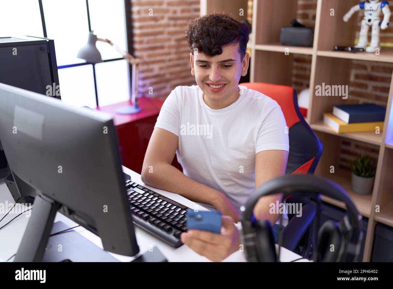 Non binary man streamer using computer and smartphone at gaming room ...
