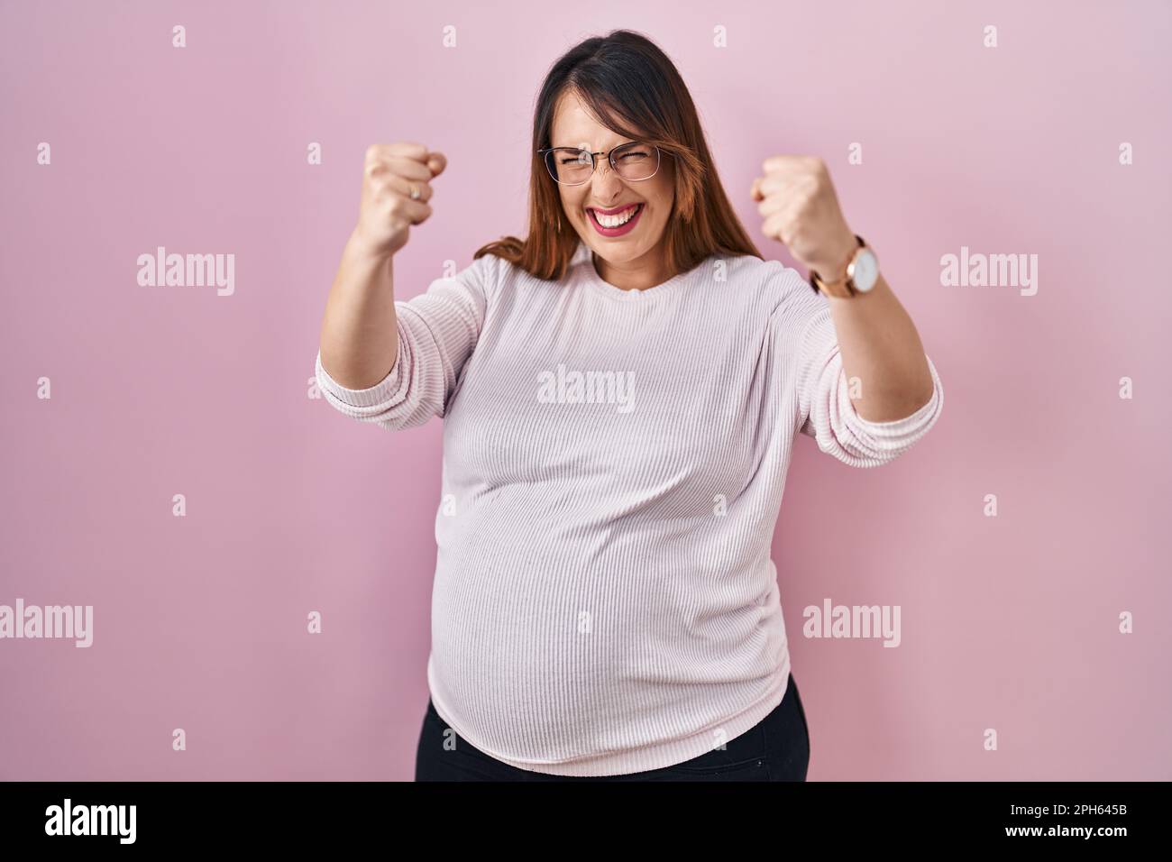 Pregnant woman standing over pink background angry and mad raising ...