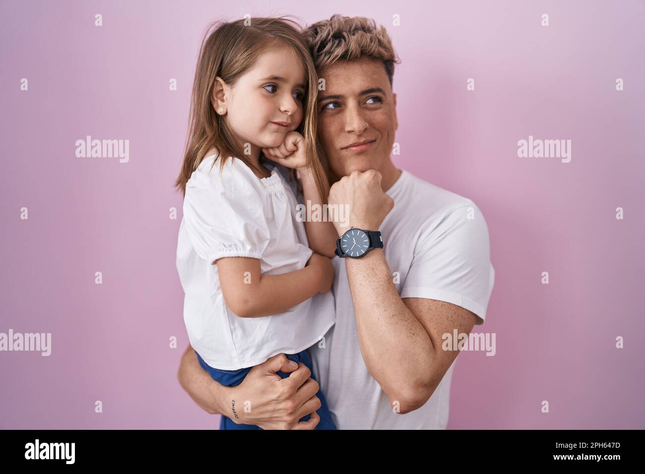 Young father hugging daughter over pink background serious face ...