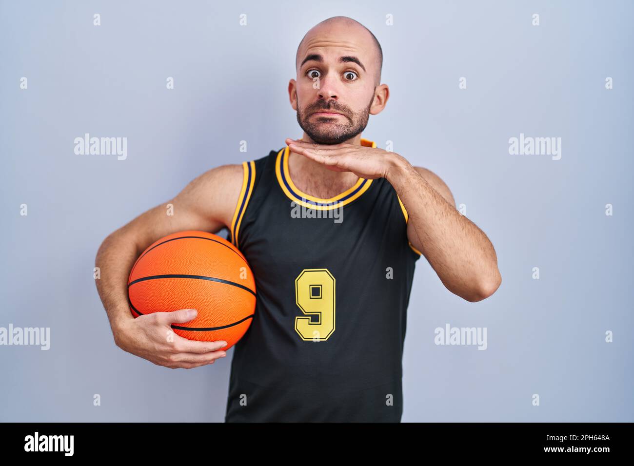 Young bald man with beard wearing basketball uniform holding ball ...