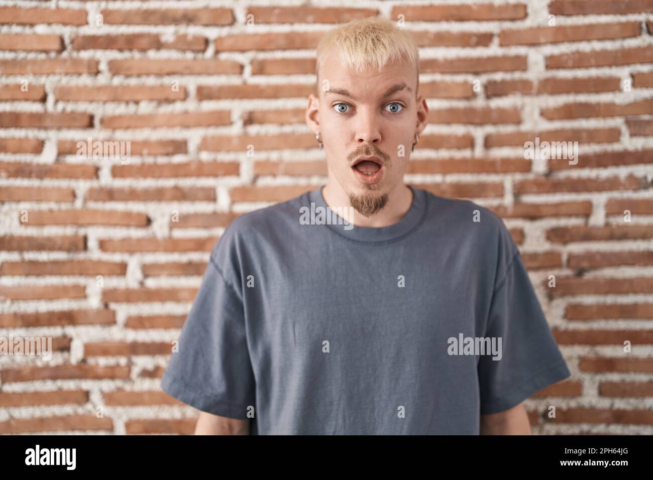 Young caucasian man standing over bricks wall afraid and shocked with ...