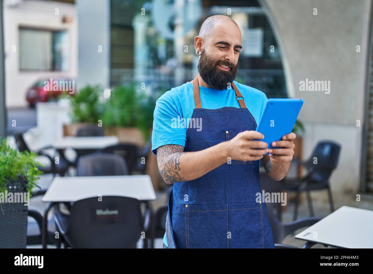 Young bald man waiter smiling confident using touchpad at coffee shop ...