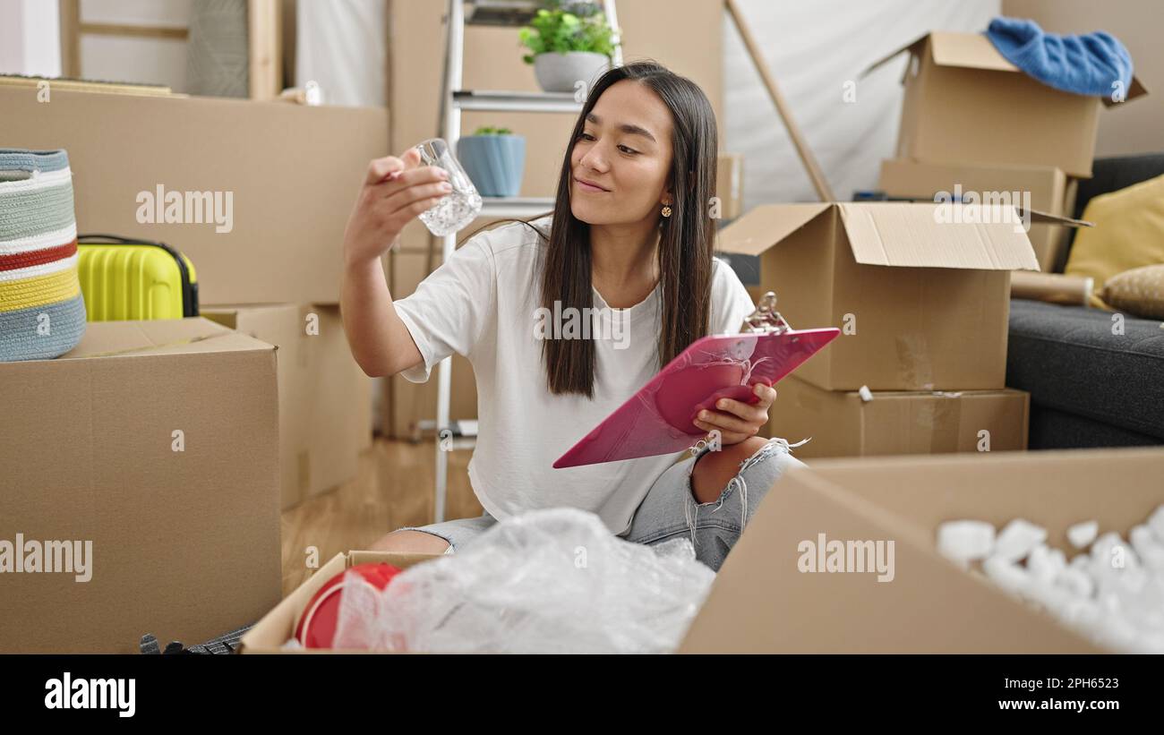 Young beautiful hispanic woman unpacking cardboard box checking on ...
