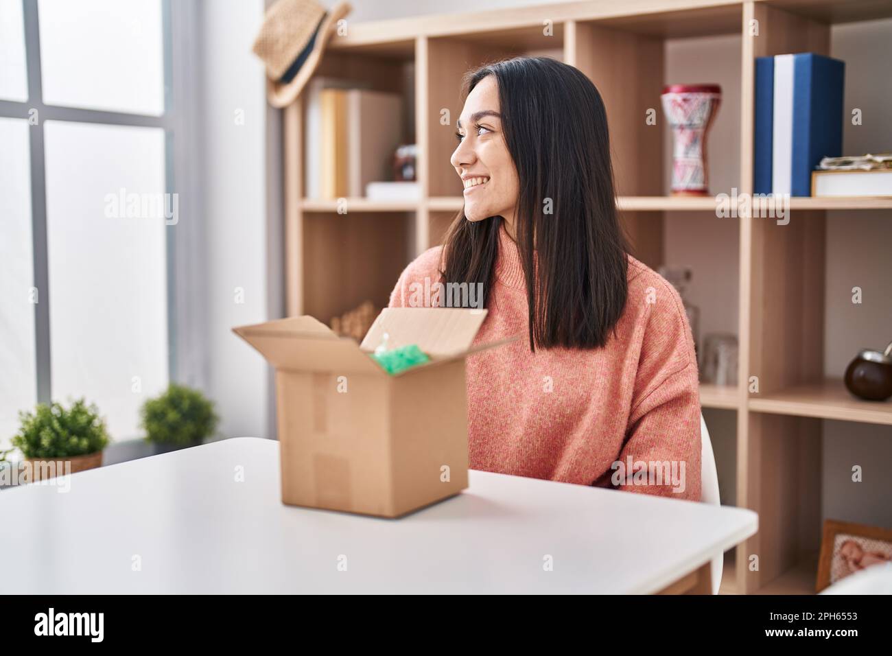 Young south asian woman opening cardboard box looking to side, relax ...