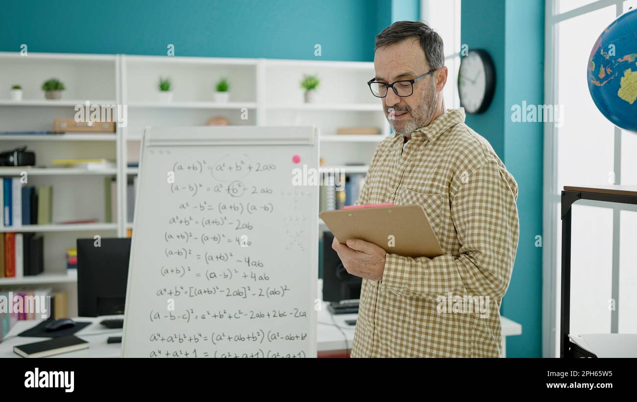 Middle age man teacher teaching lesson reading document at classroom ...