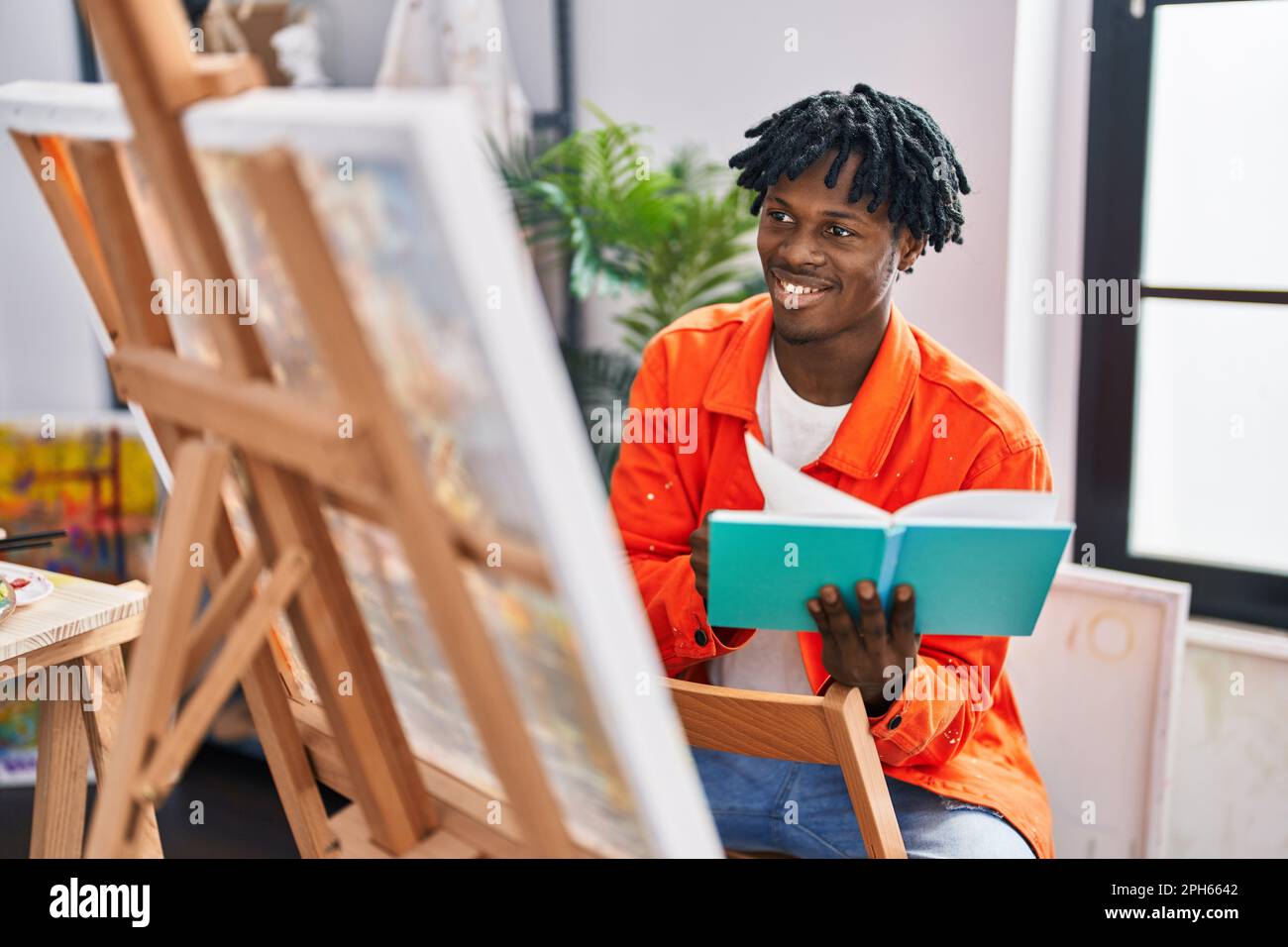 African american man artist smiling confident reading book drawing at ...