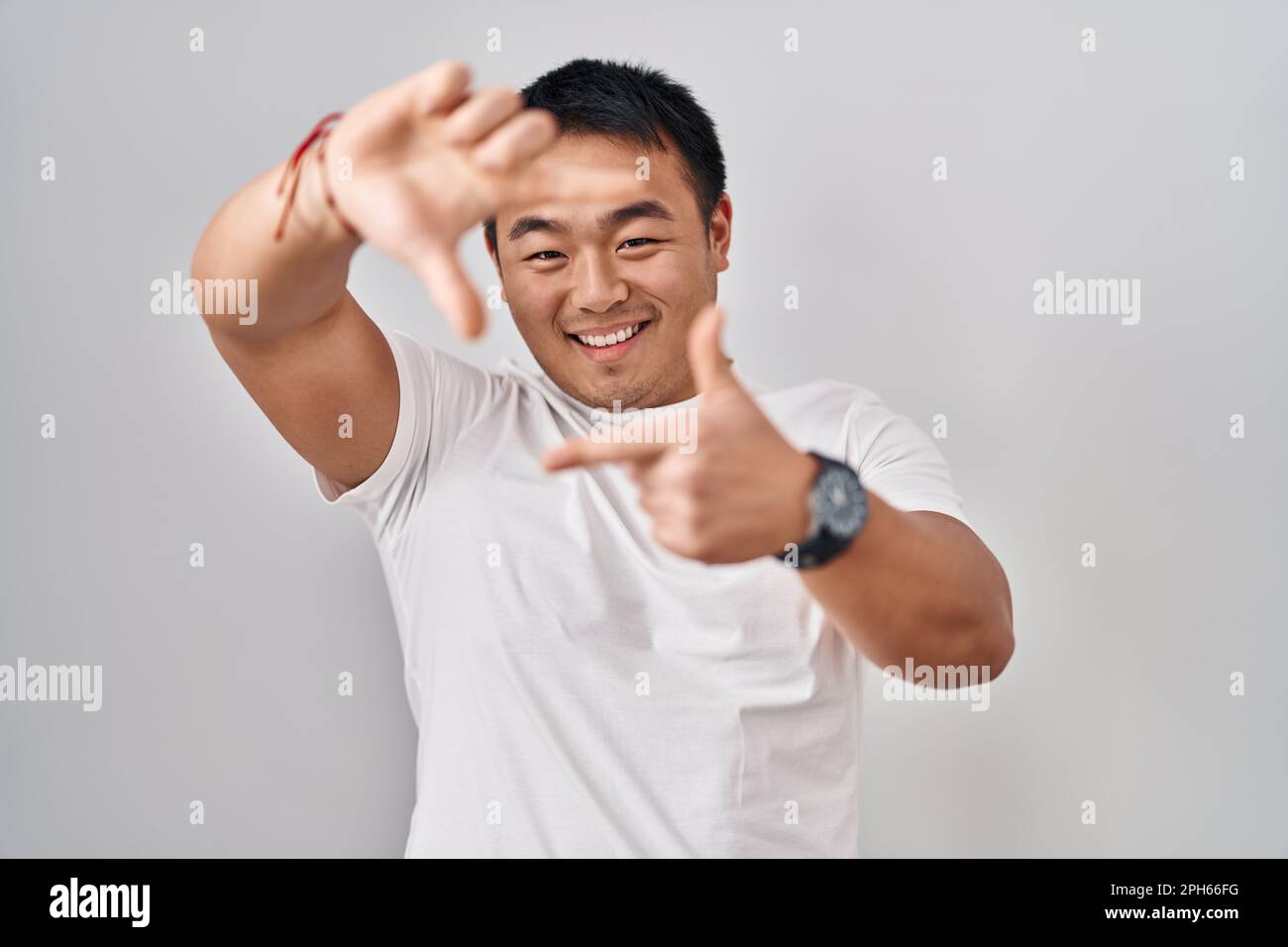 Young chinese man standing over white background smiling making frame ...