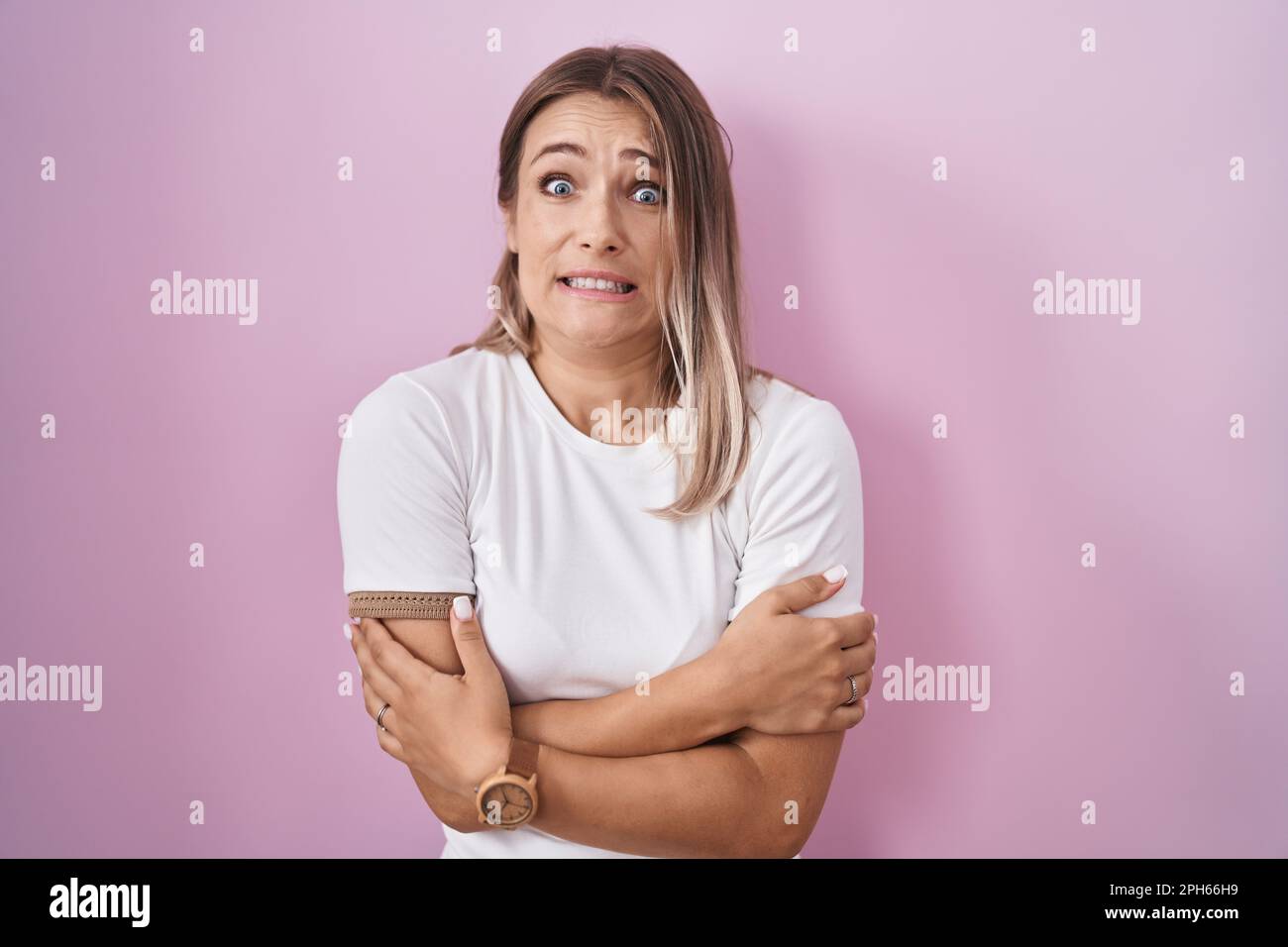 Blonde caucasian woman standing over pink background shaking and ...