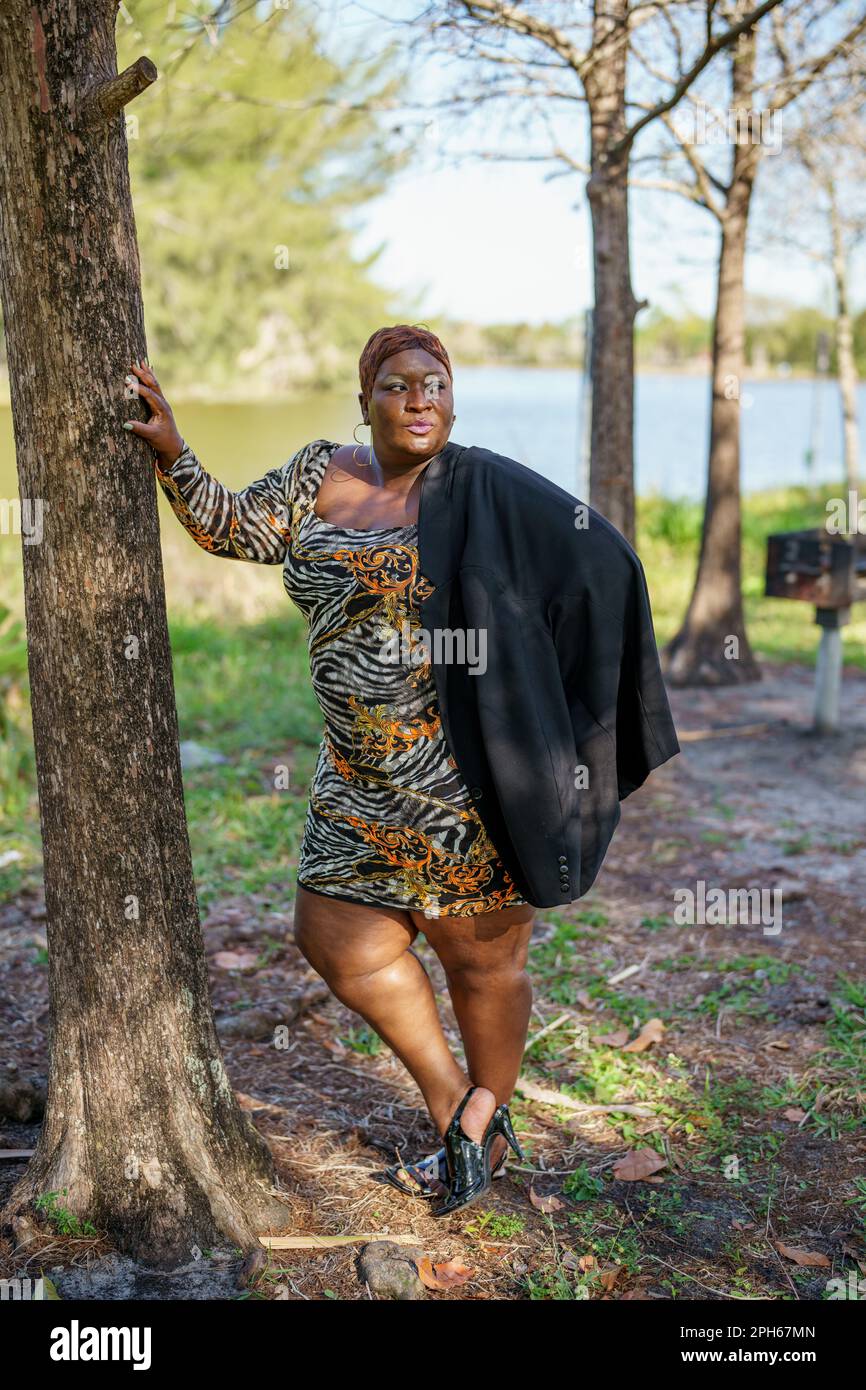 Beautiful black plus sized model posing by a tree in a tranquil park ...