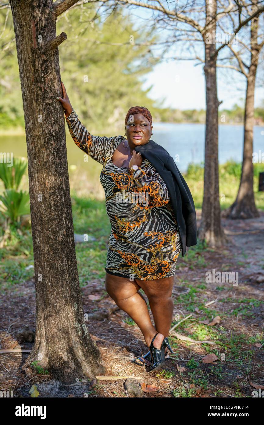 Beautiful black plus sized model posing by a tree in a tranquil park ...