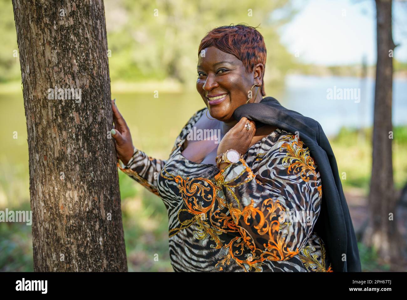 Beautiful black plus sized model posing by a tree in a tranquil park ...