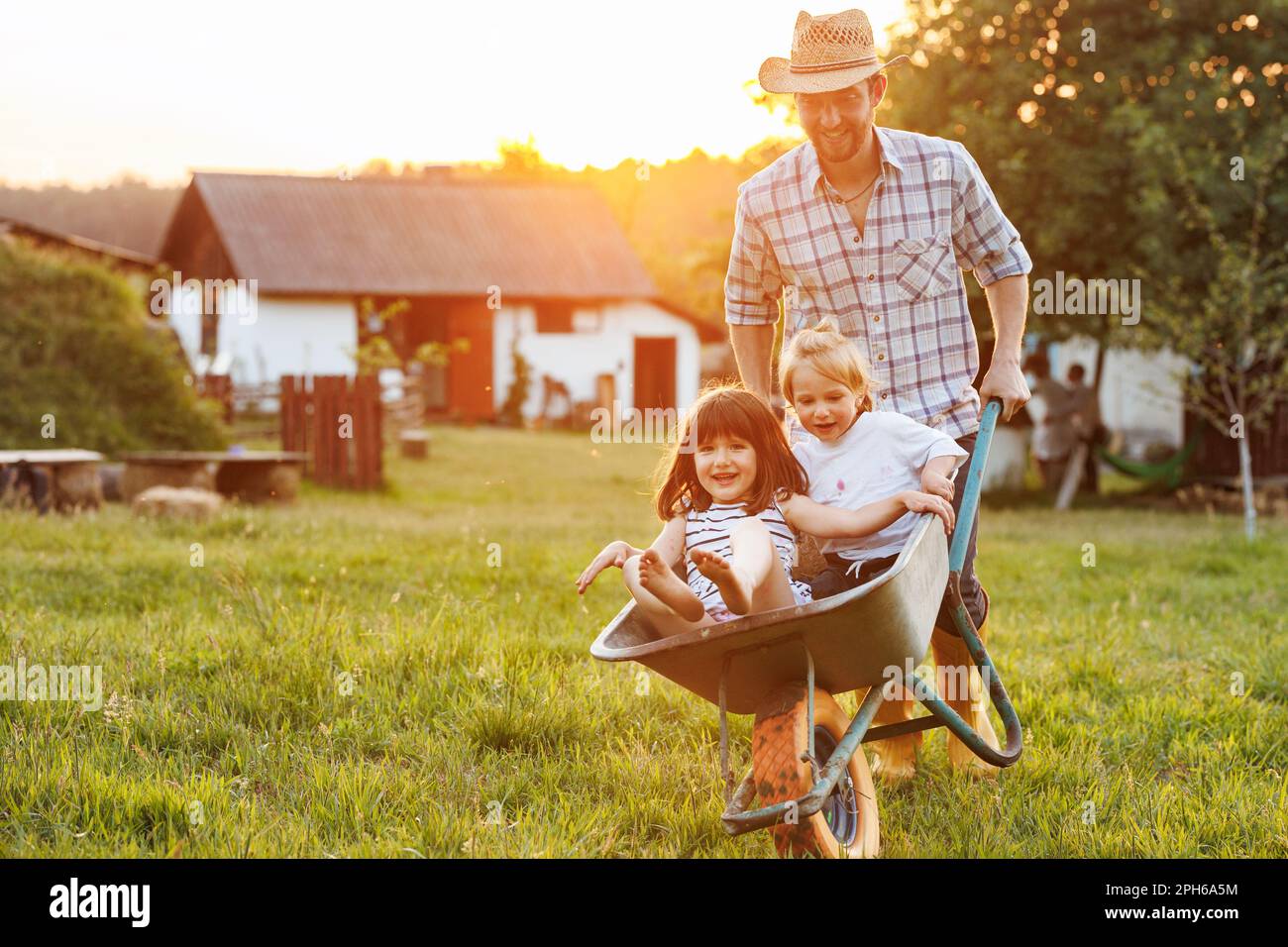 Happy little children having fun in a wheelbarrow pushing by dad in ...
