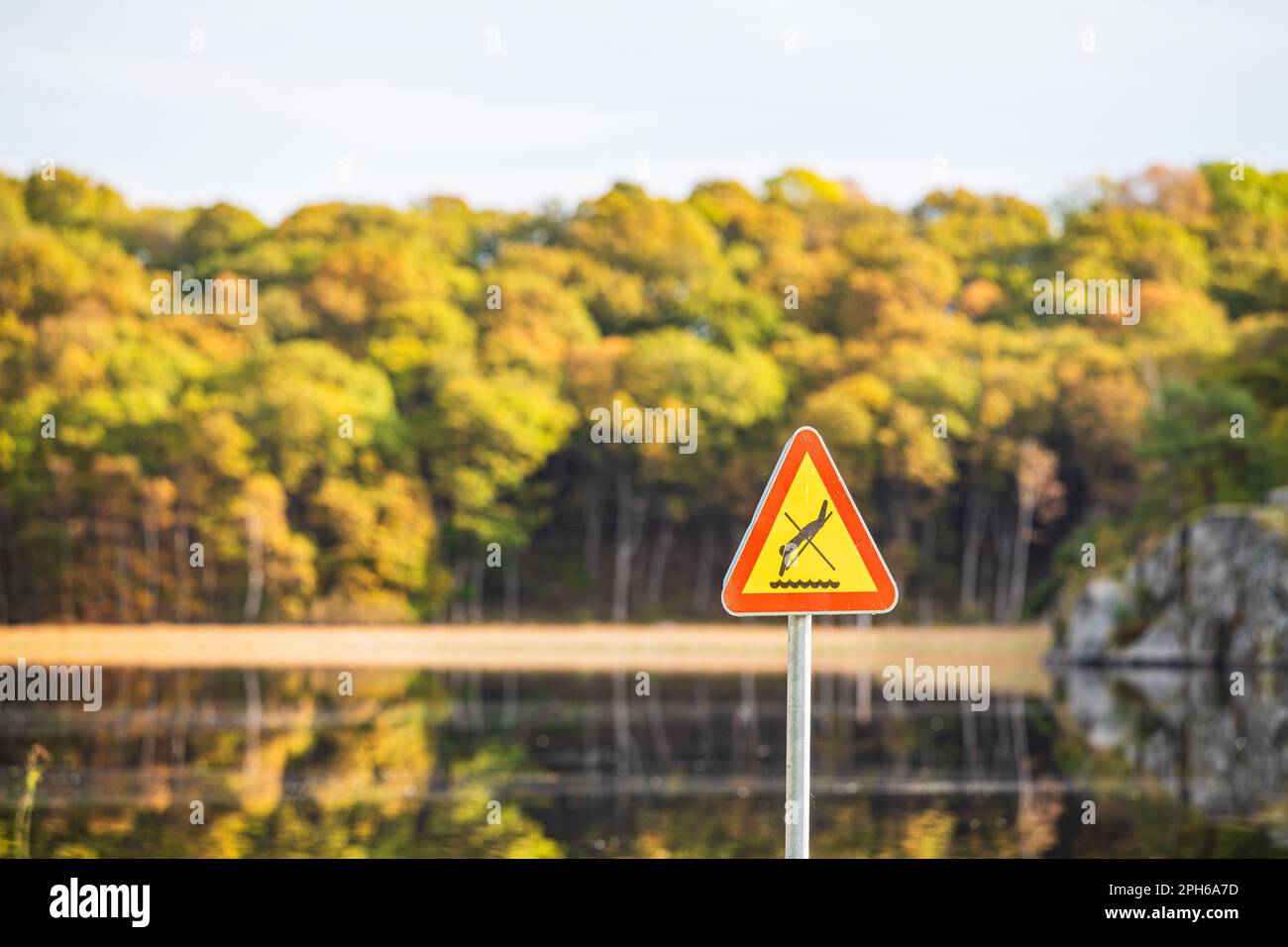 A bright yellow triangle-shaped warning sign prohibiting diving in a ...
