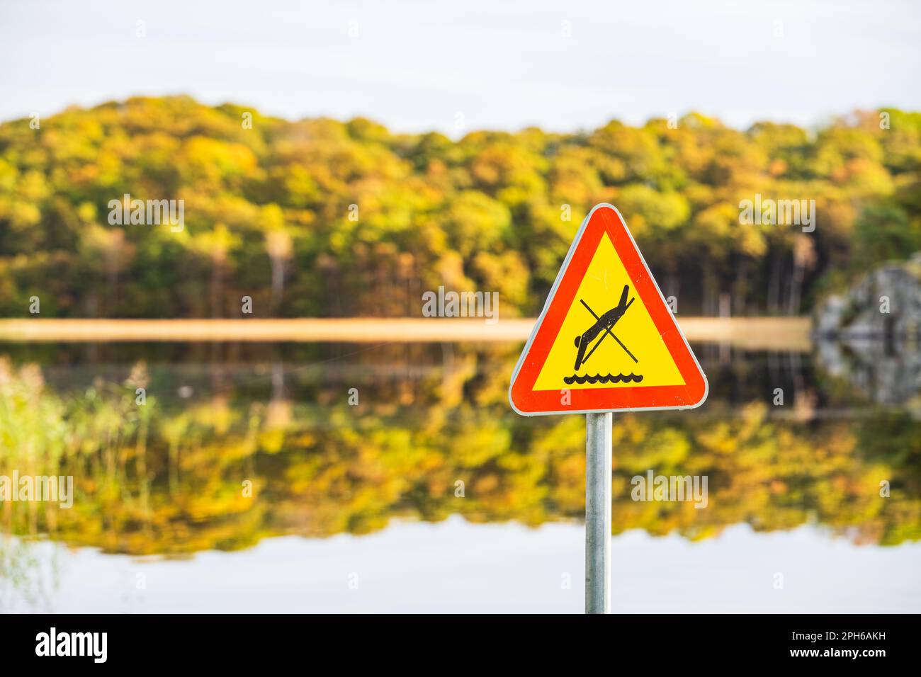 A bright yellow triangle-shaped warning sign prohibiting diving in a ...