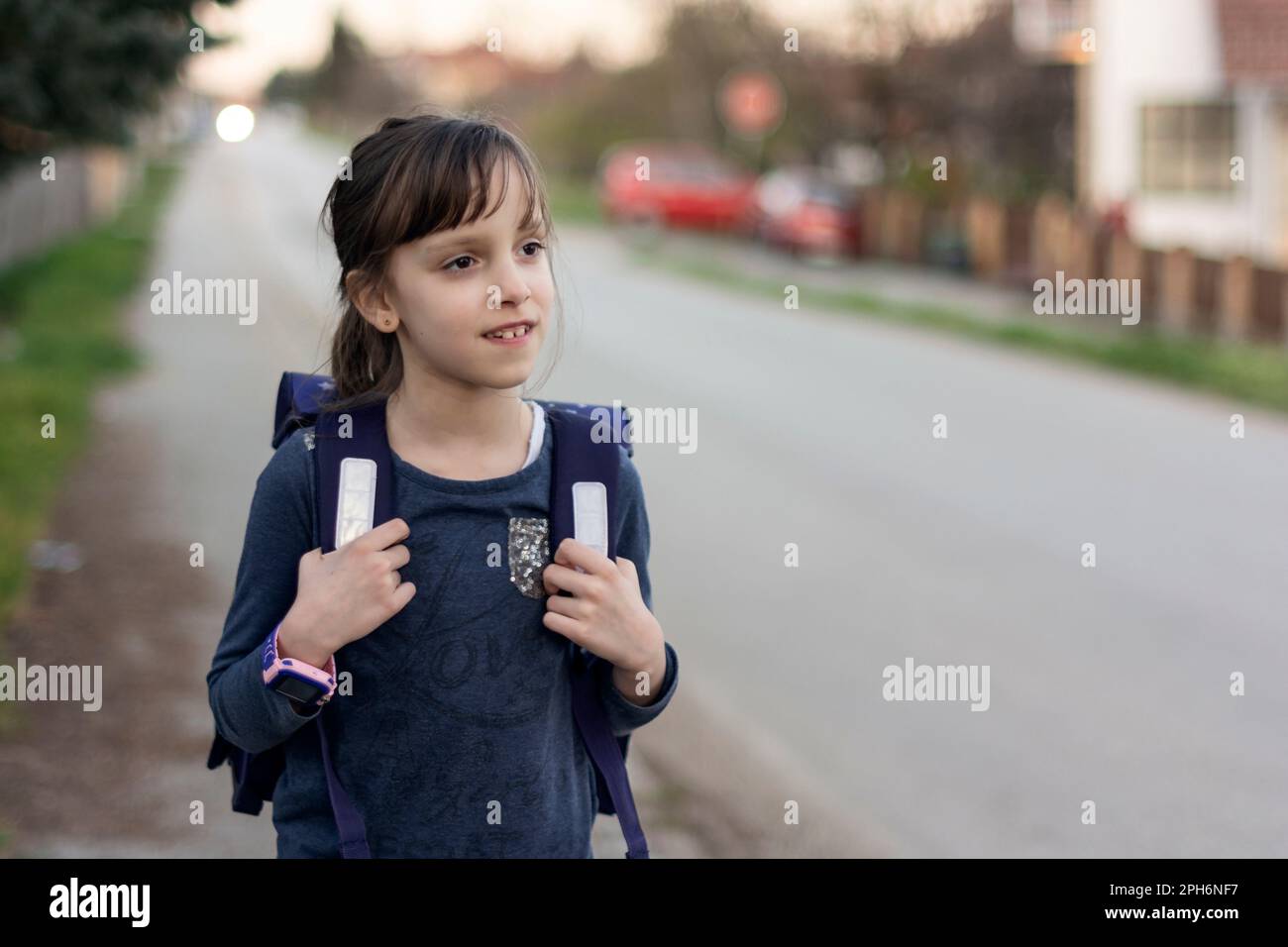 Portrait of smiling elementary school girl with her backpack walks down ...