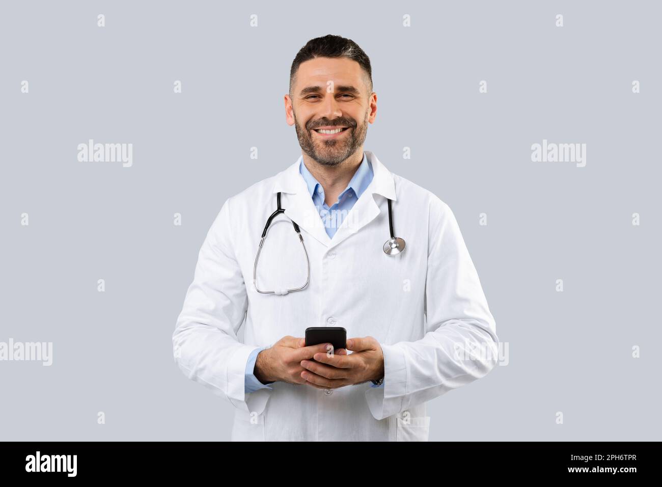 Portrait of friendly male therapist in white coat and with stethoscope ...