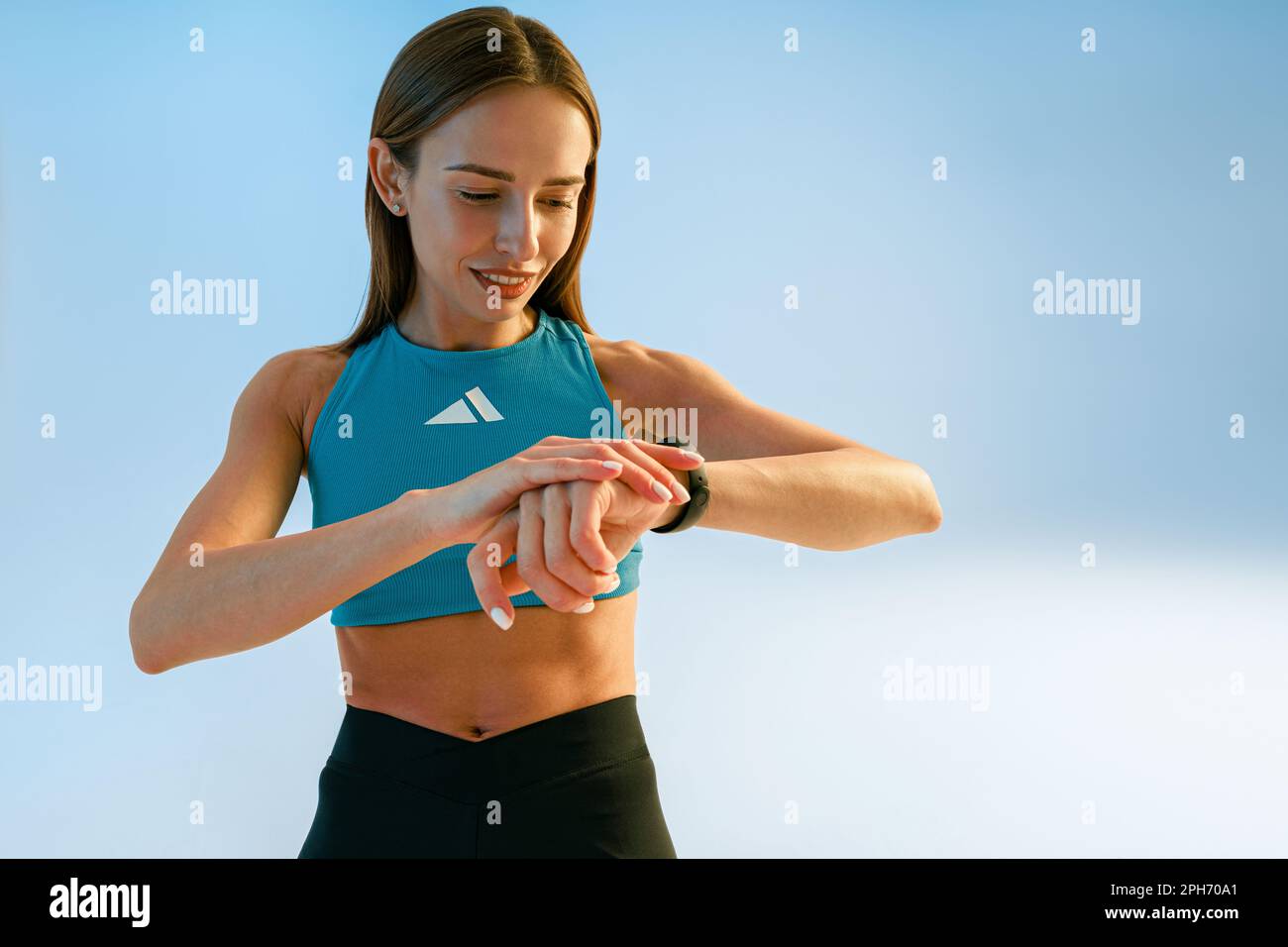 Smiling sporty woman standing and looking at watch checking her ...