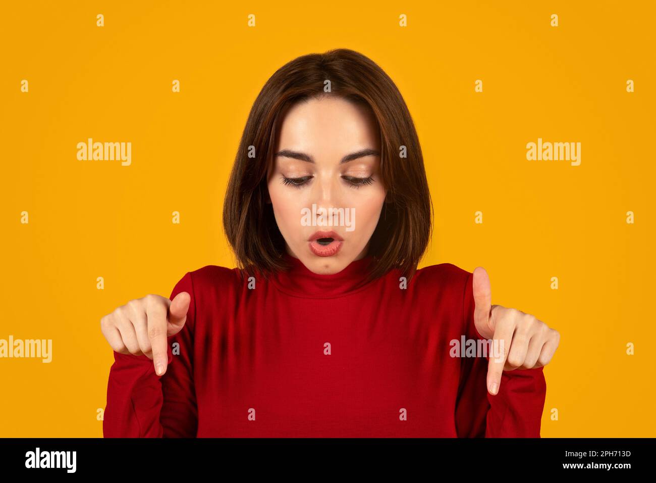 Amazed young lady pointing down, orange background Stock Photo - Alamy