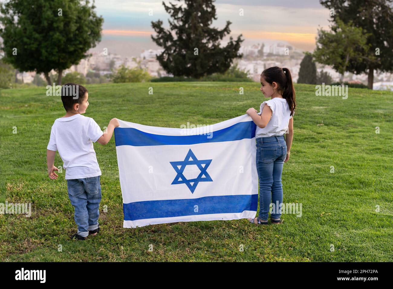 Young children stand on a hill holding an Israeli flag. A rear view ...
