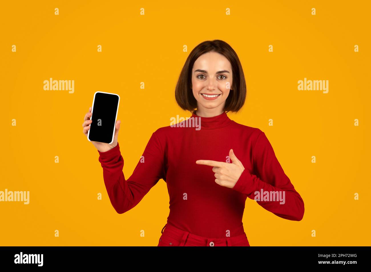 Cheerful pretty young woman pointing at cell phone, mockup Stock Photo ...