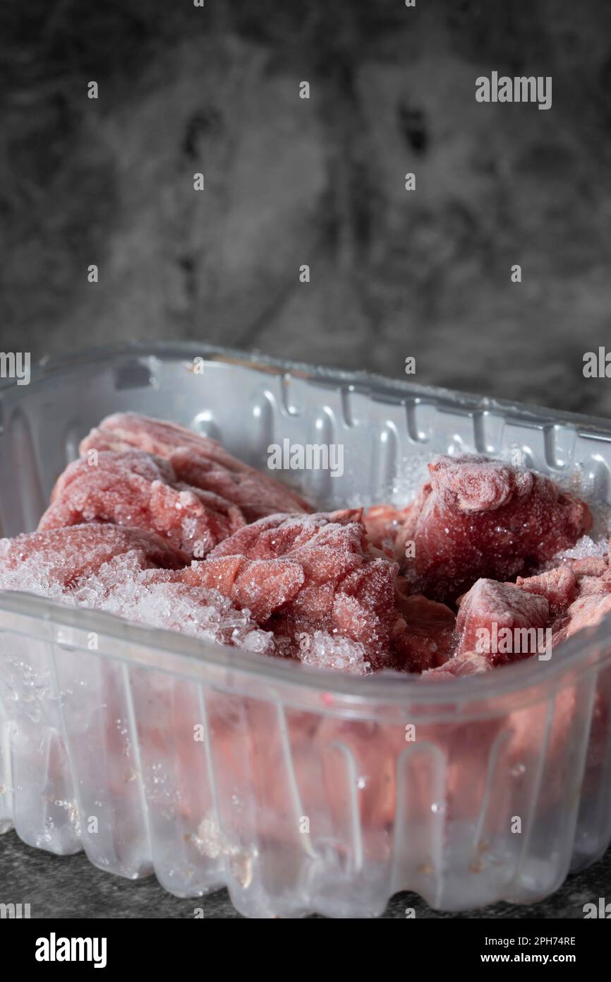 Frozen lean beef steak cubes in clear plastic tray packaging. On a dark ...